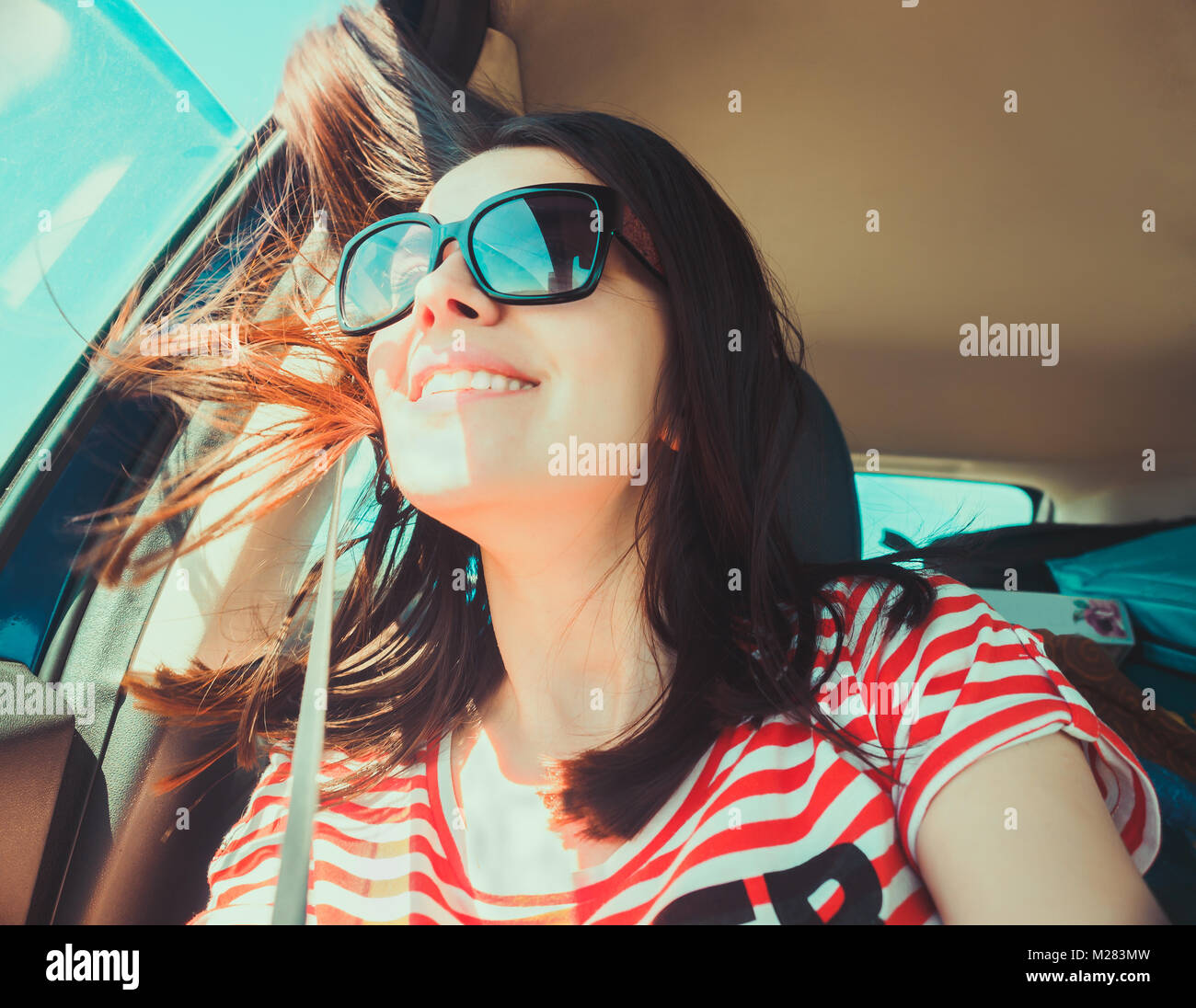 Cute young girl is looking out the window of a car laughing. Hair ...