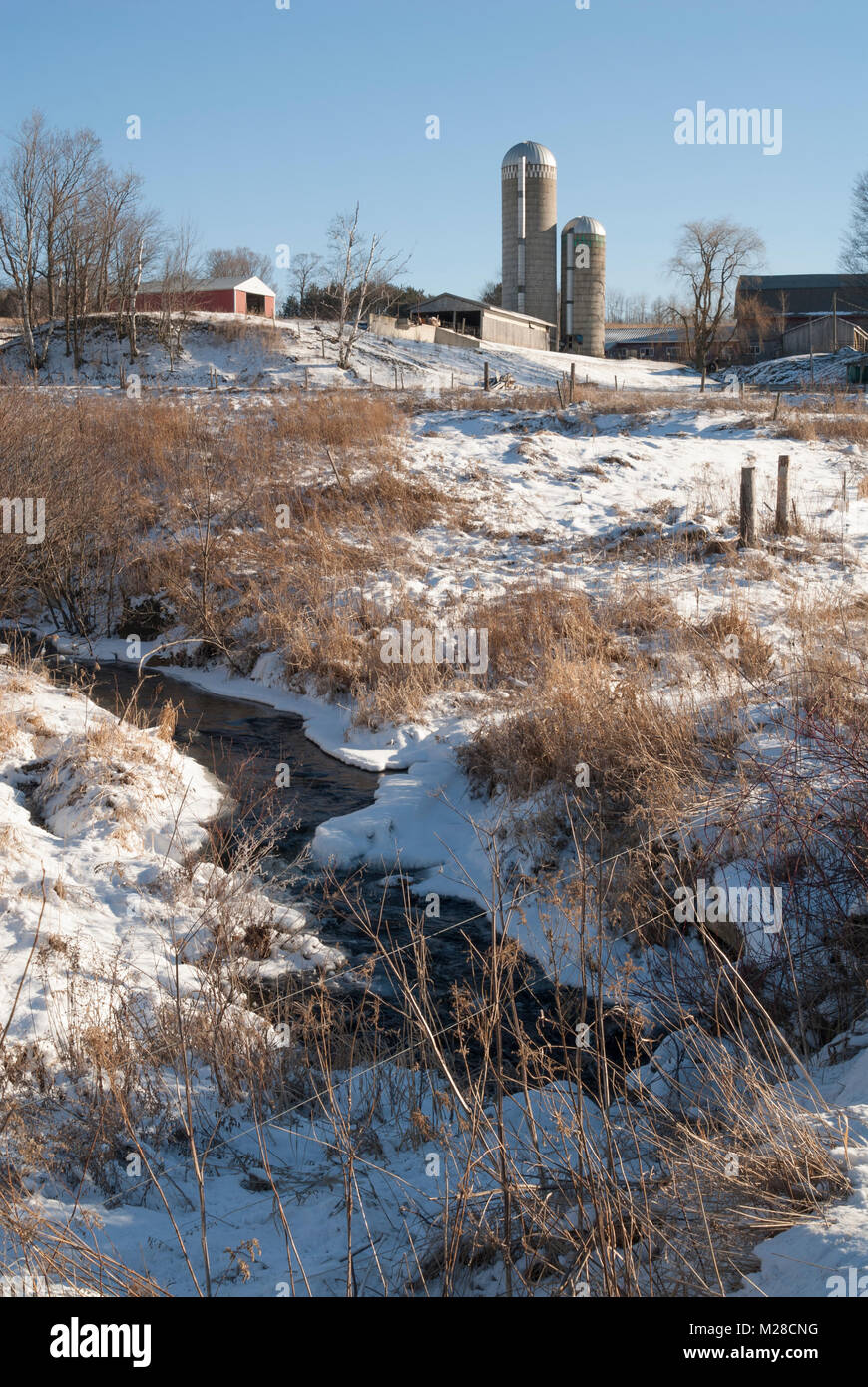 Winter farm scene with silos and stream cutting through the snow in the ...