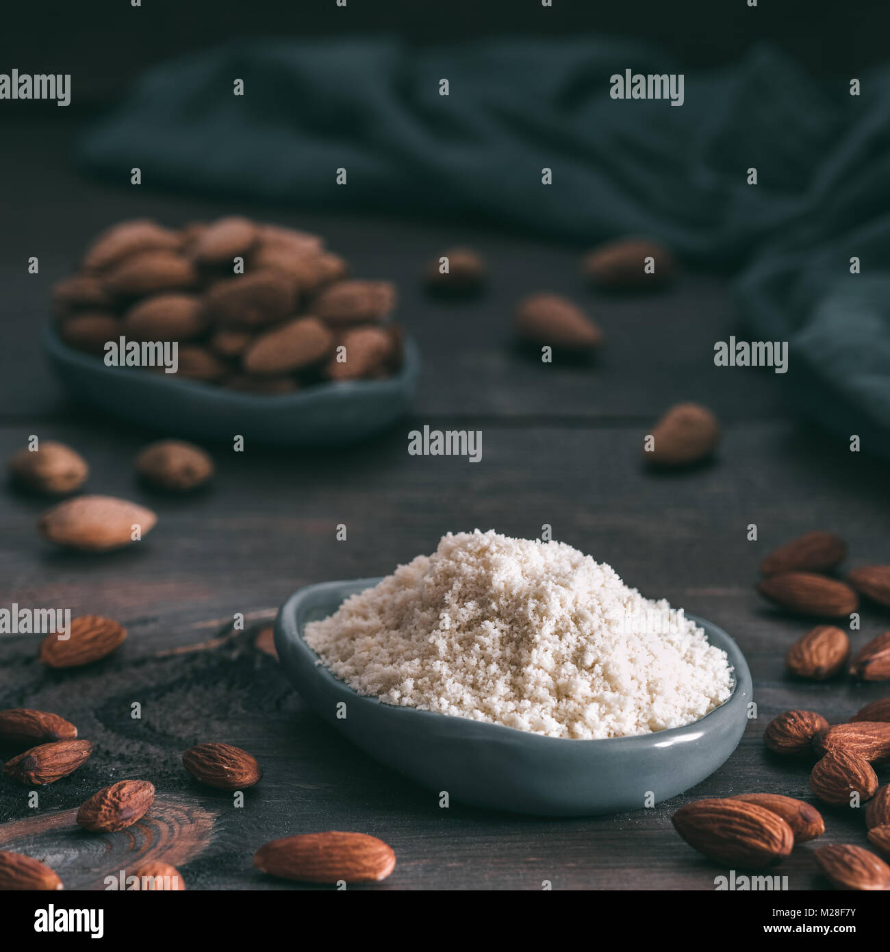 Almond powder in gray trendy plate and almonds on dark wooden table ...