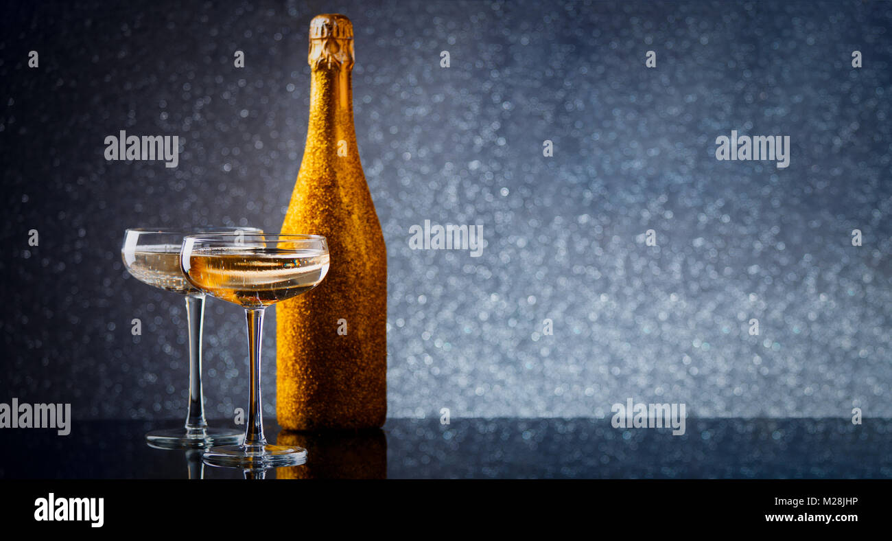 Photo of bottle of wine in gold wrapper with two wine glasses on gray ...