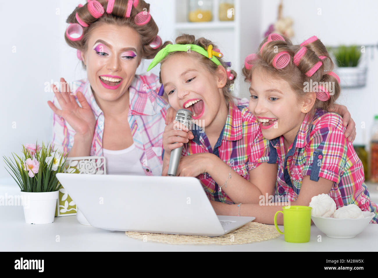 mother and daughters sitting at table with laptop and singing karaoke ...