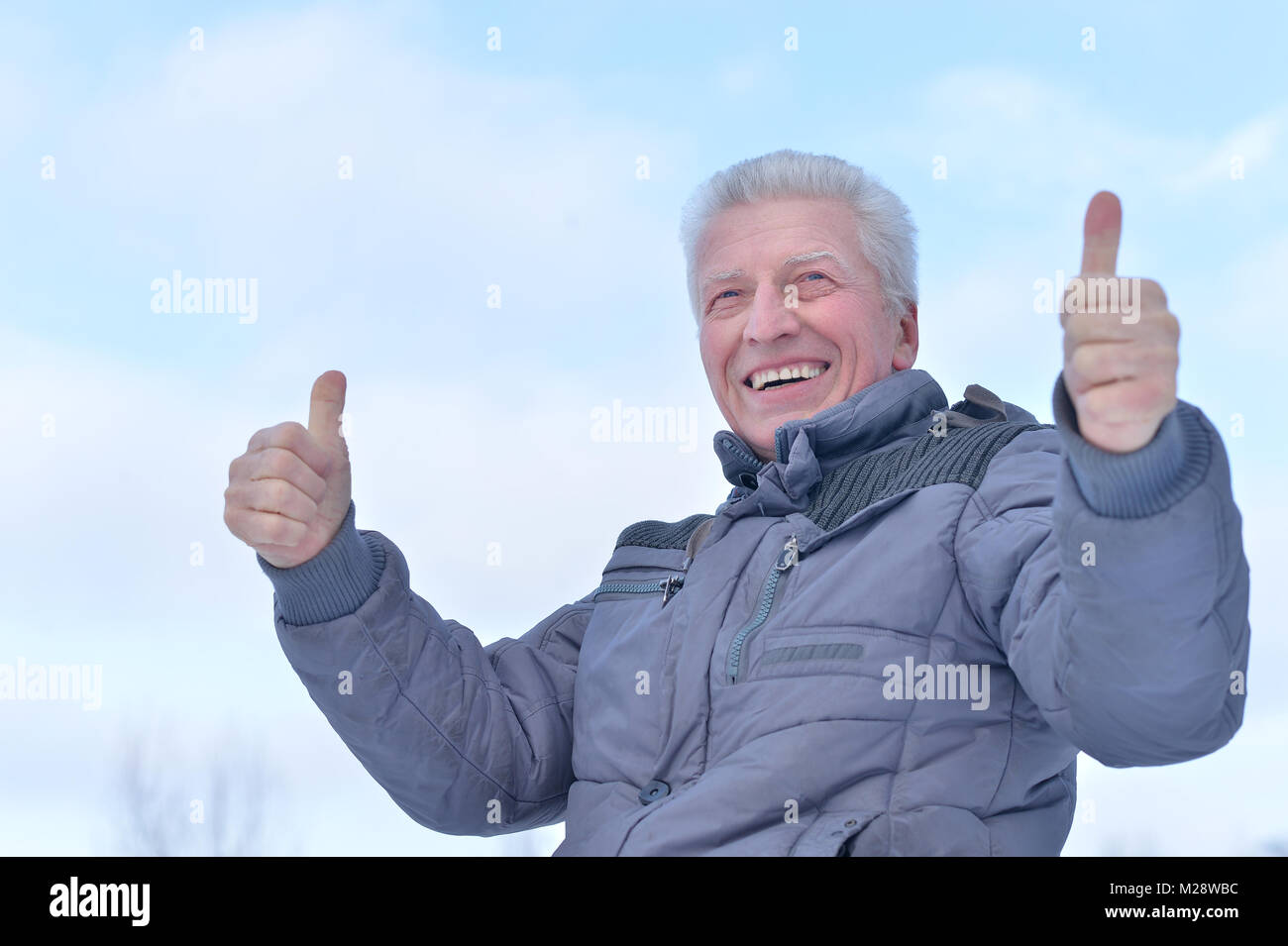 Portrait of smiling senior man standing outdoors in winter and showing ...