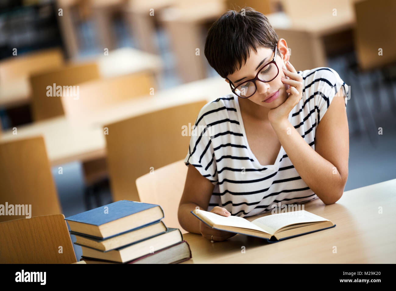 Female student reading a book at library Stock Photo - Alamy