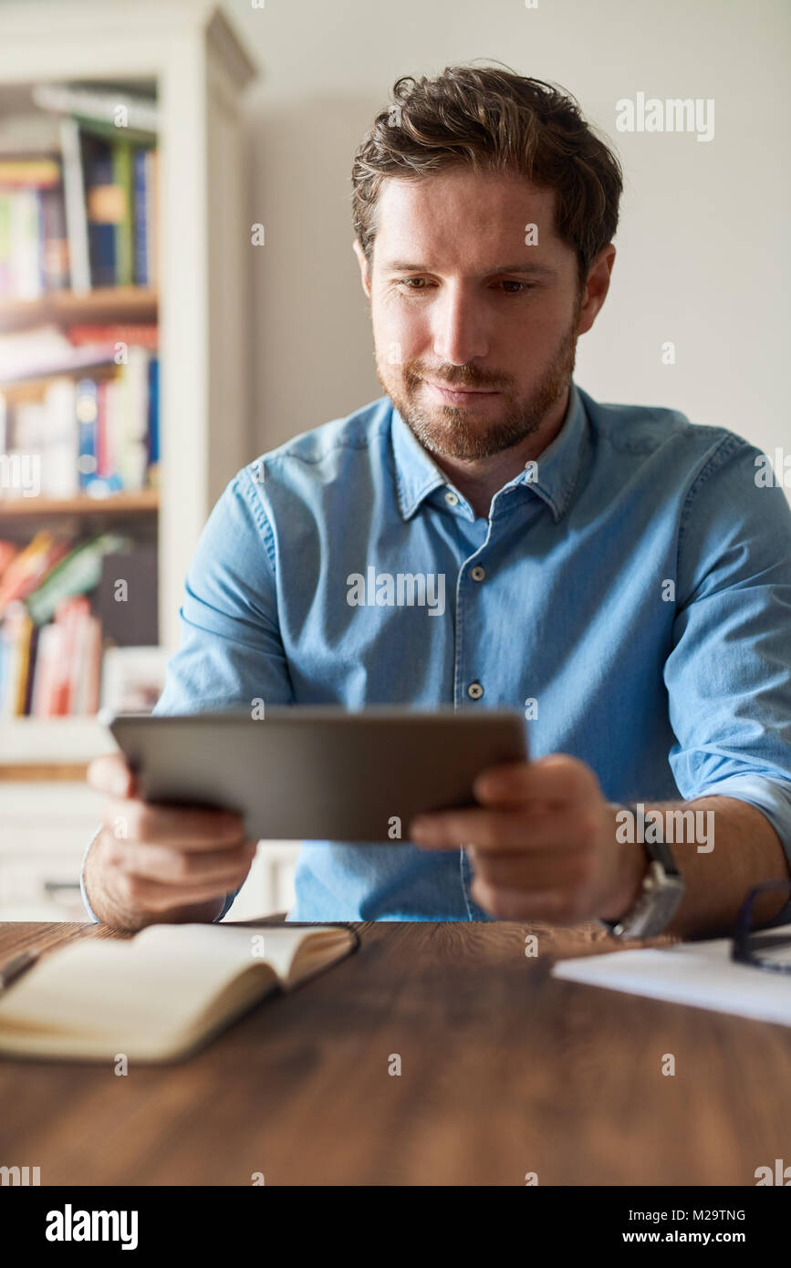 Young man sitting at a table in his living room working online with a ...