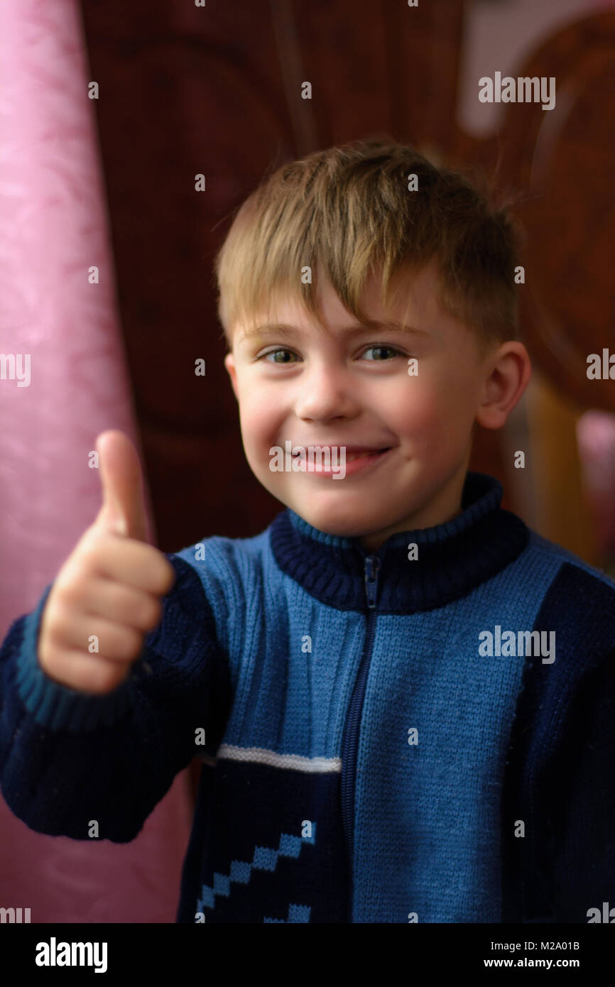 A smiling Ukrainian boy showA cute boy shows a sign ok in a blue jumper ...
