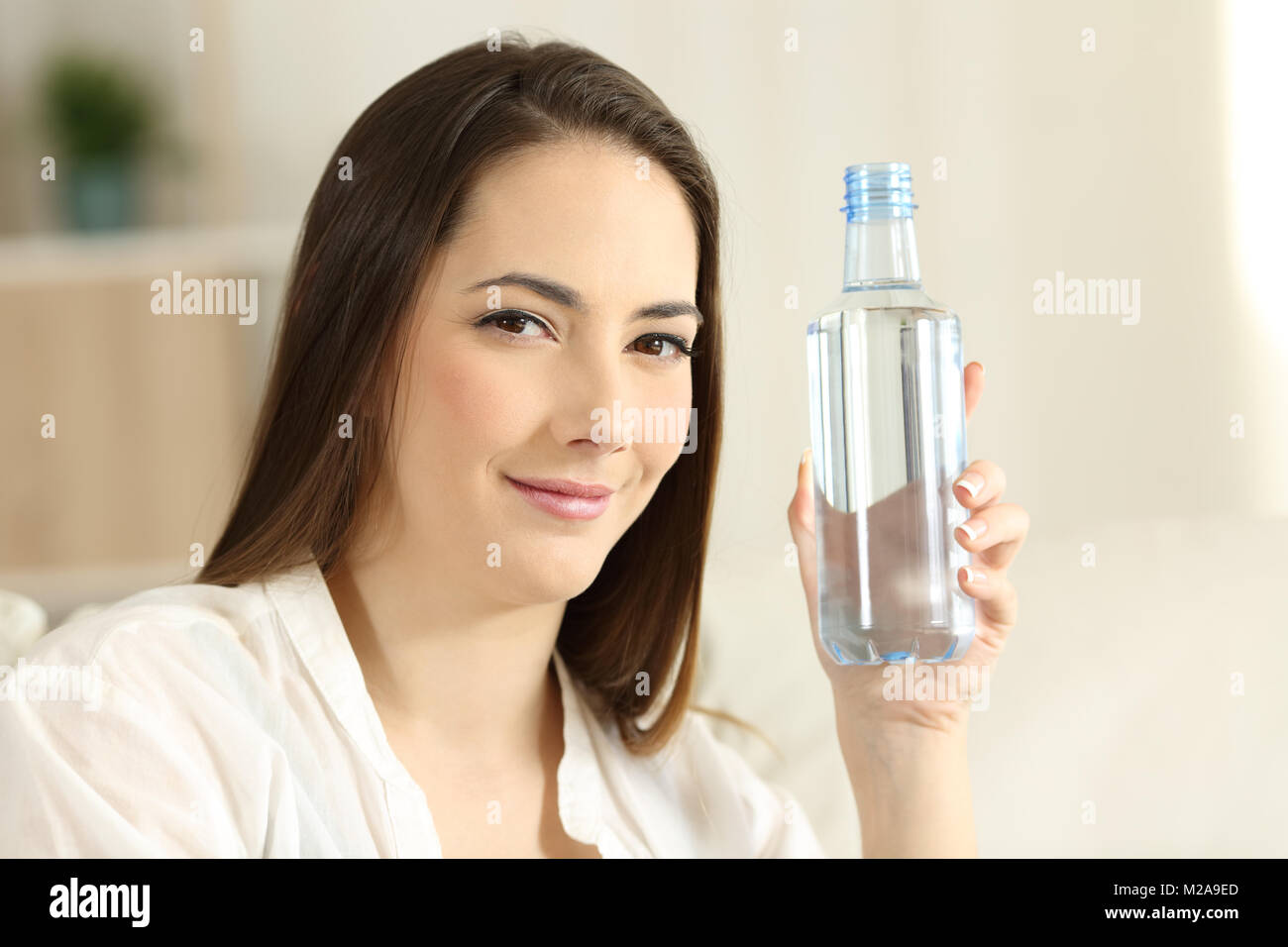 Portrait of a relaxed girl showing a generic water bottle at home Stock ...