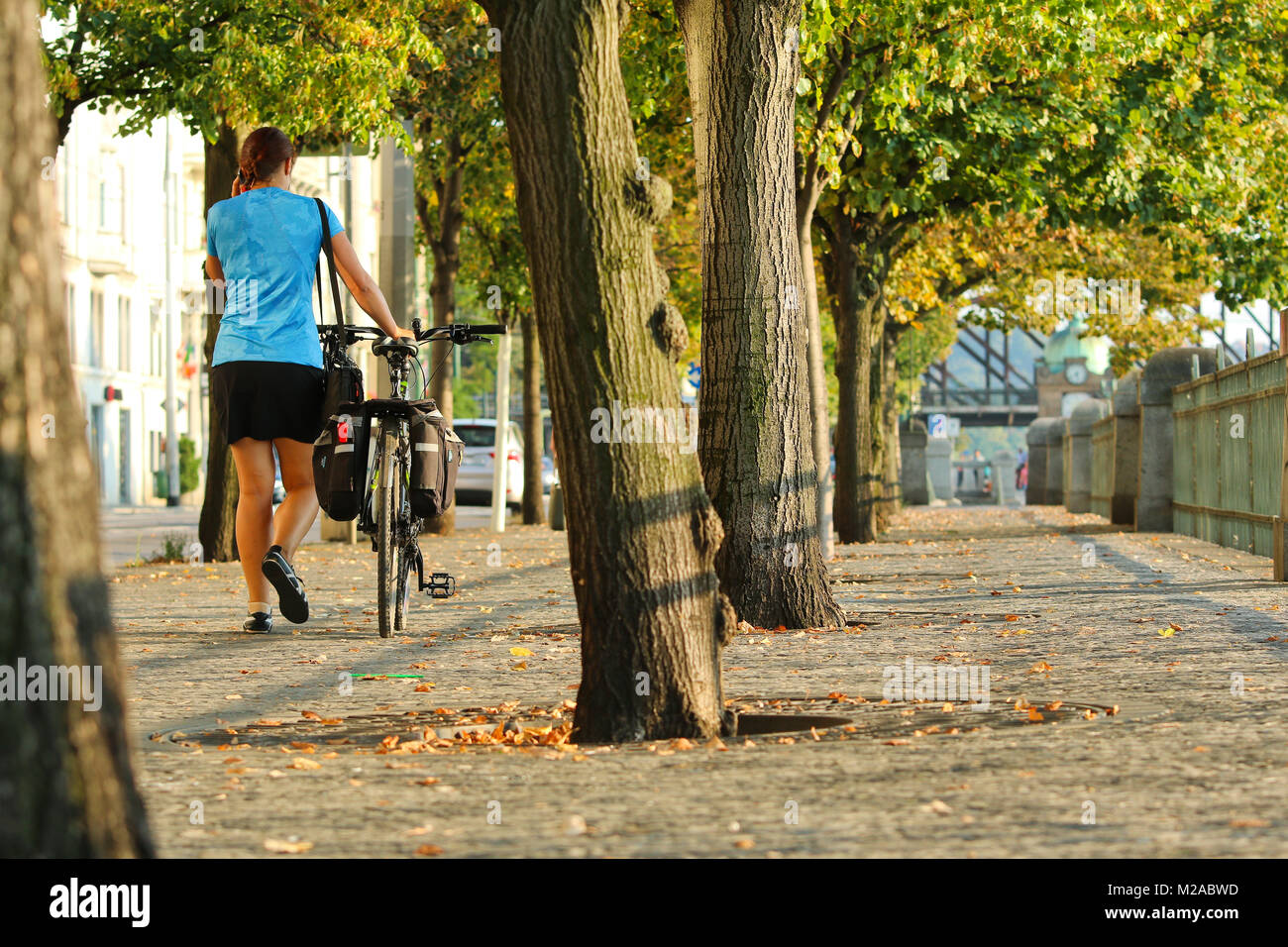 A cyclist is walking on the pathway, pushing the bike. I is a sunny day ...