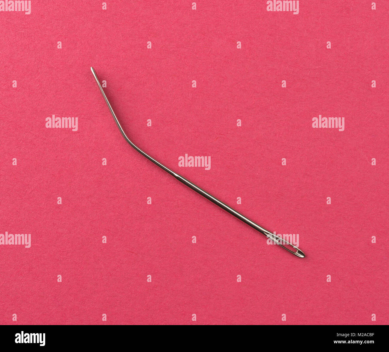 Top view of an angled heavy duty upholstery cloth needle on a red paper ...