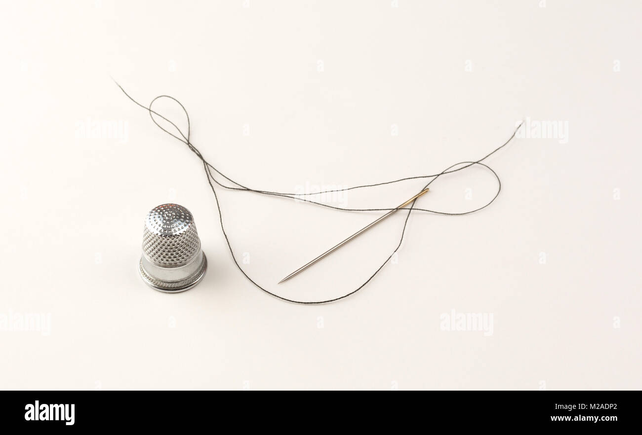 An old metal sewing thimble and long threaded needle with string on ...
