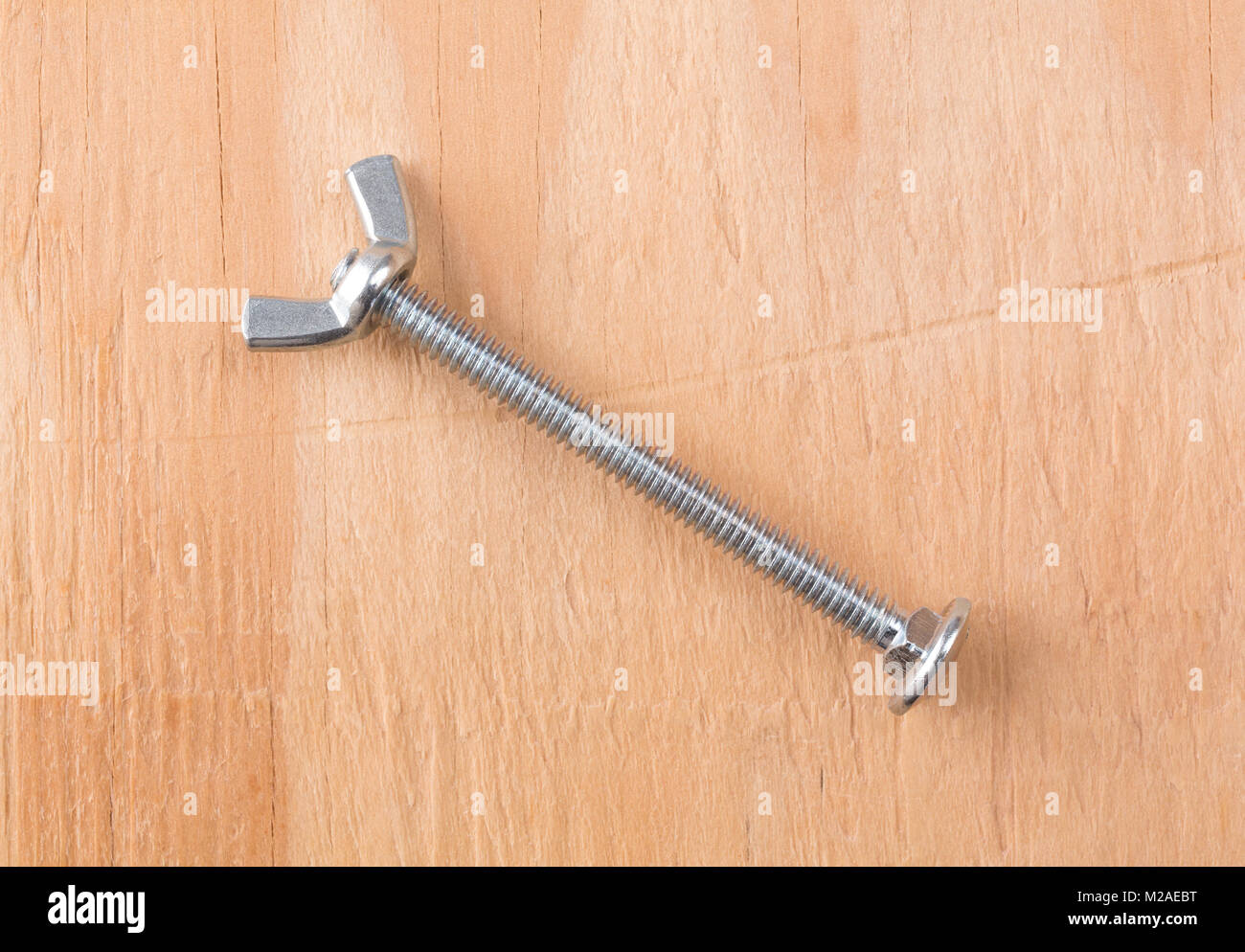 Top view of a wing nut threaded onto a long bolt atop a plywood surface ...