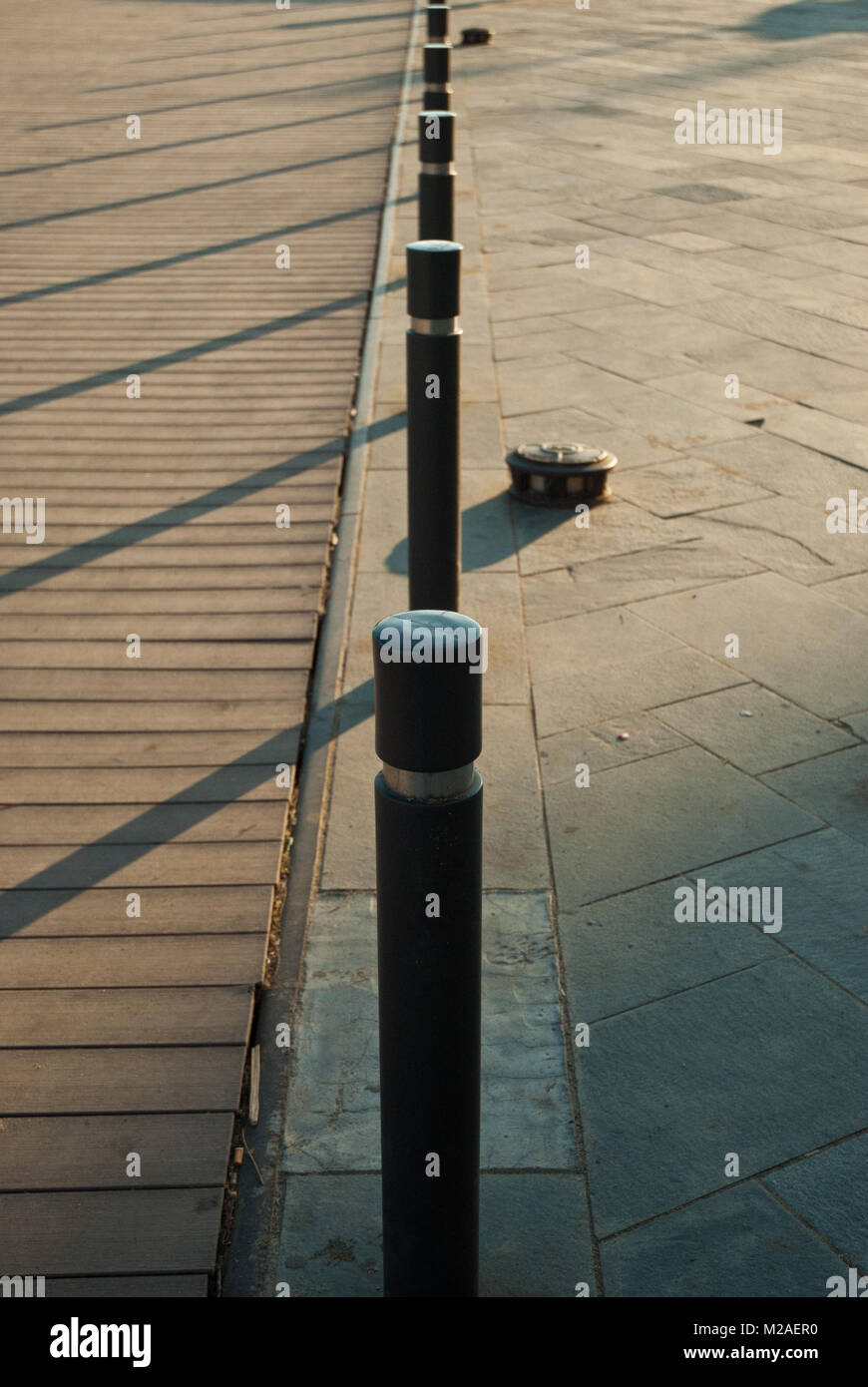 A line of bollards casting long shadows across a boardwalk in Barcelona ...