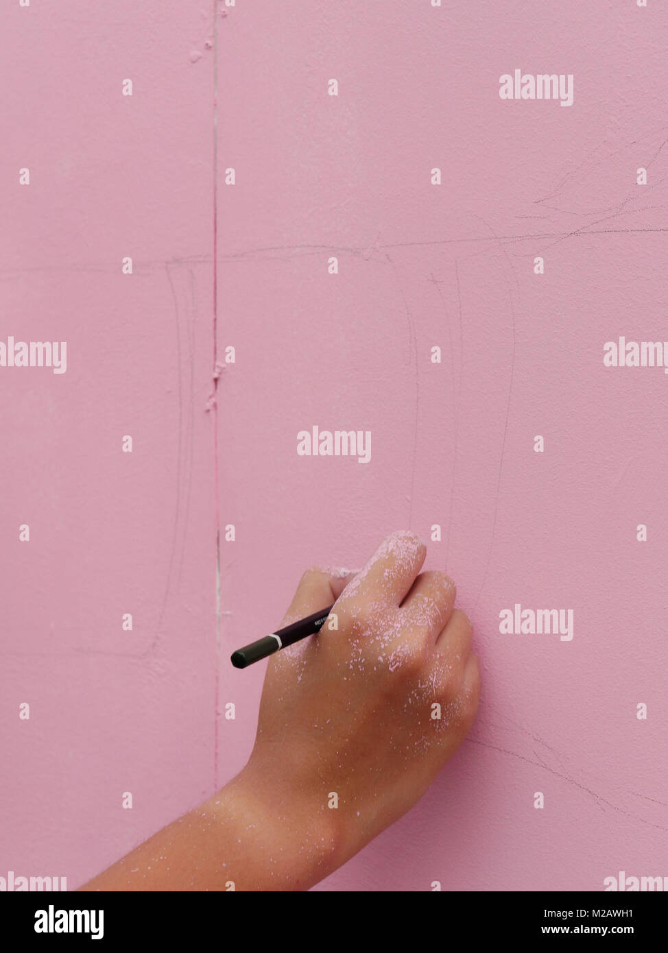 An artist hand with a pencil sketching the art work on the pink wall ...