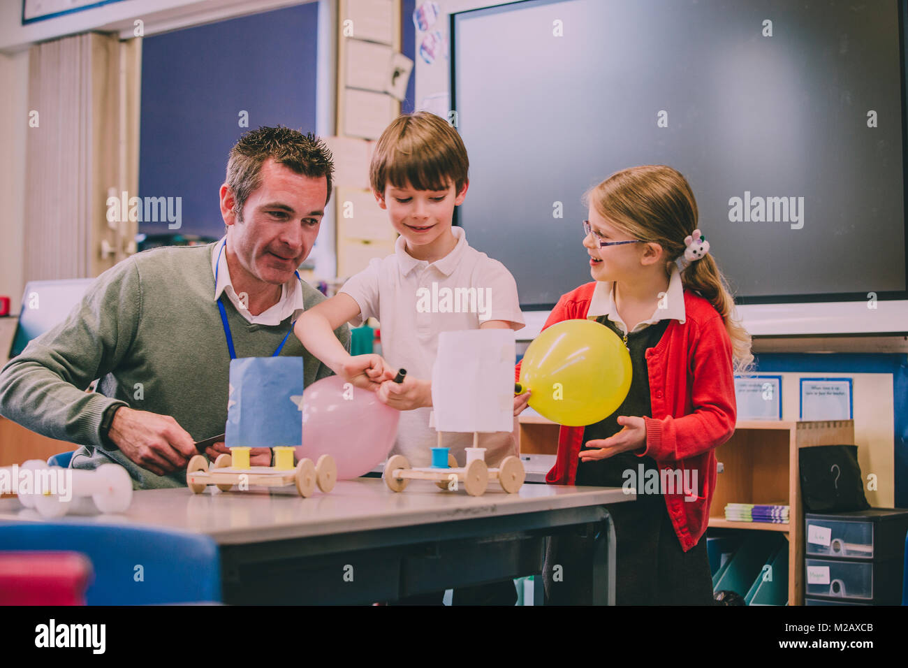 Primary school teacher is helping two of his students with a STEM ...