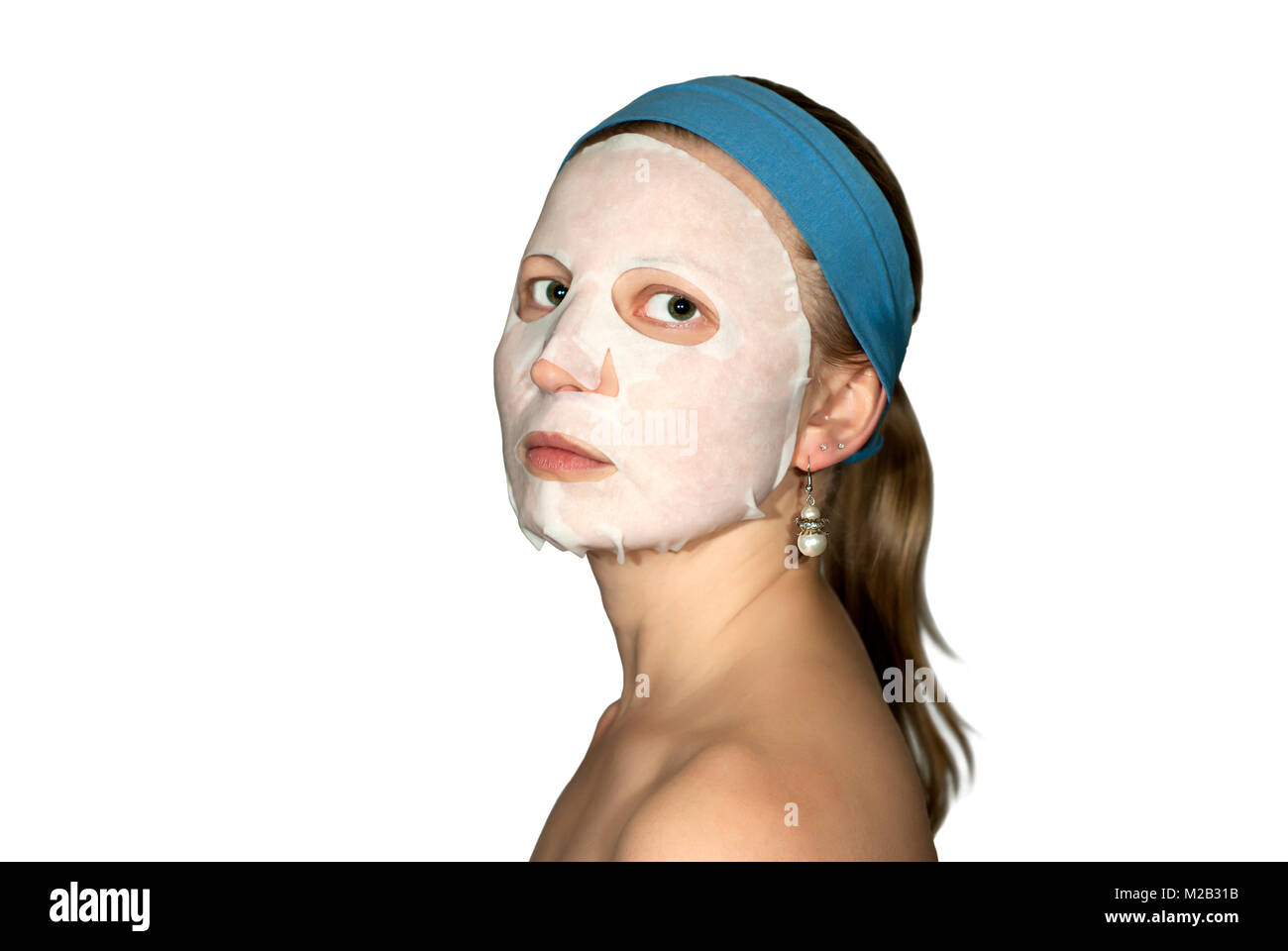 Girl with facial paper mask for cosmetic procedure looking at camera on ...