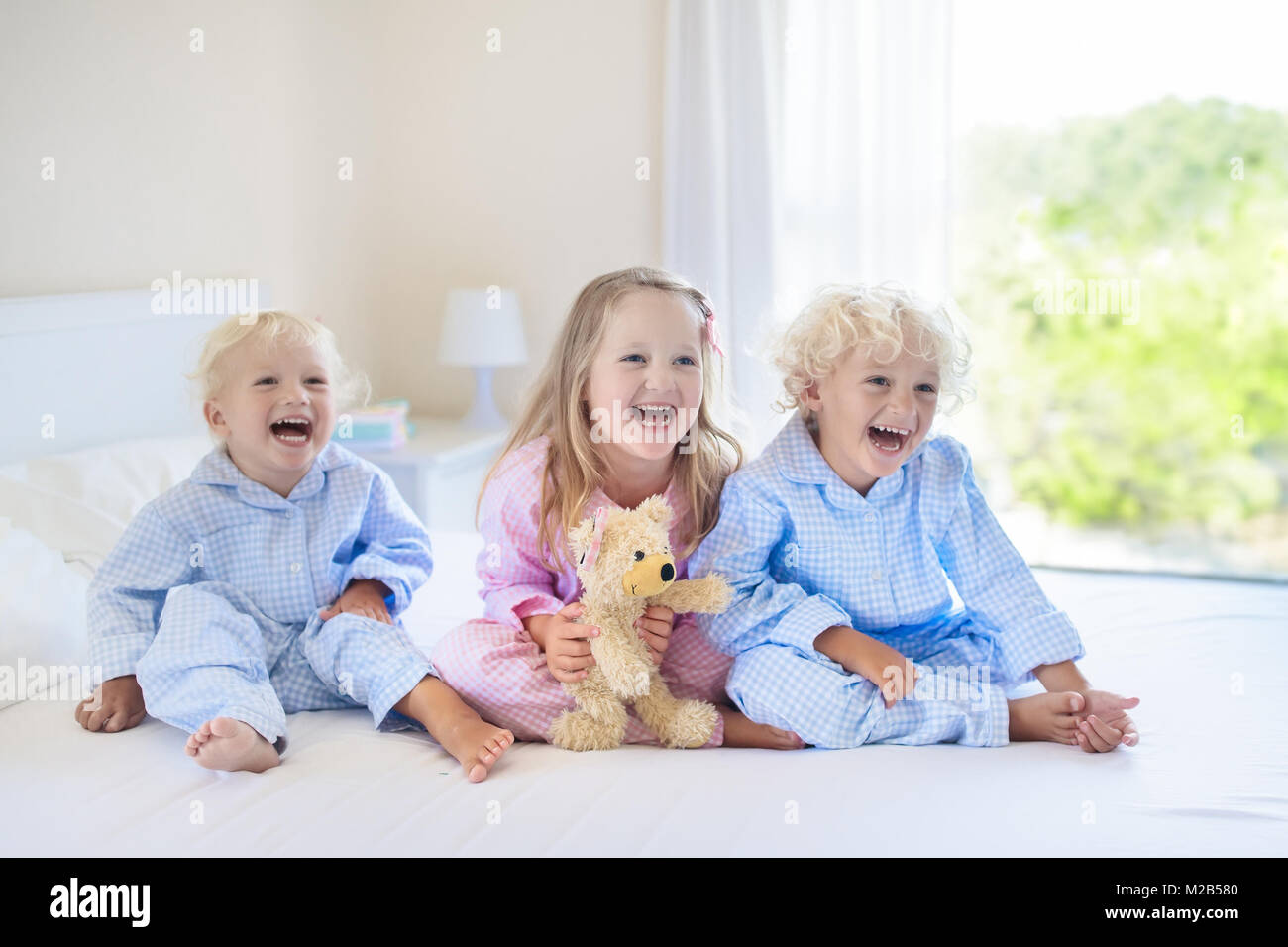 Kids playing in parents bed. Children wake up in sunny white bedroom ...