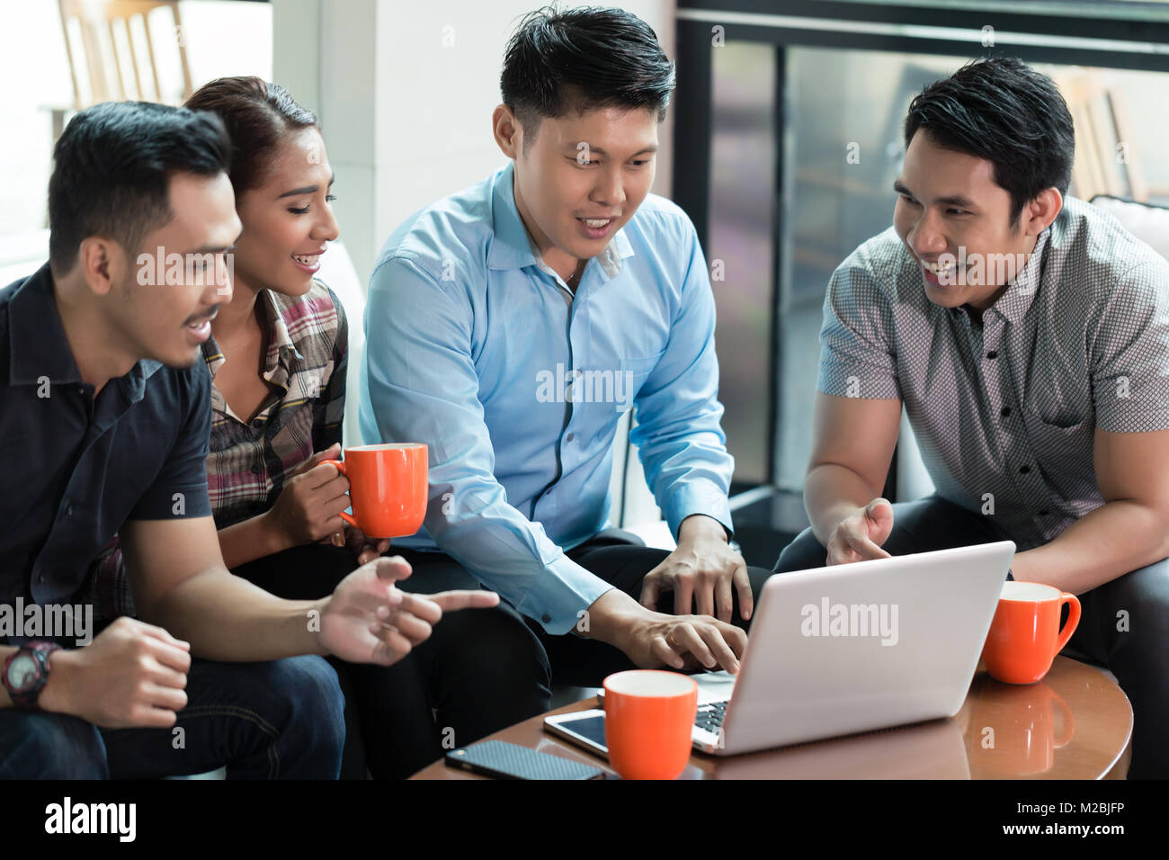 Two cheerful Chinese young men using a laptop while sharing business ...
