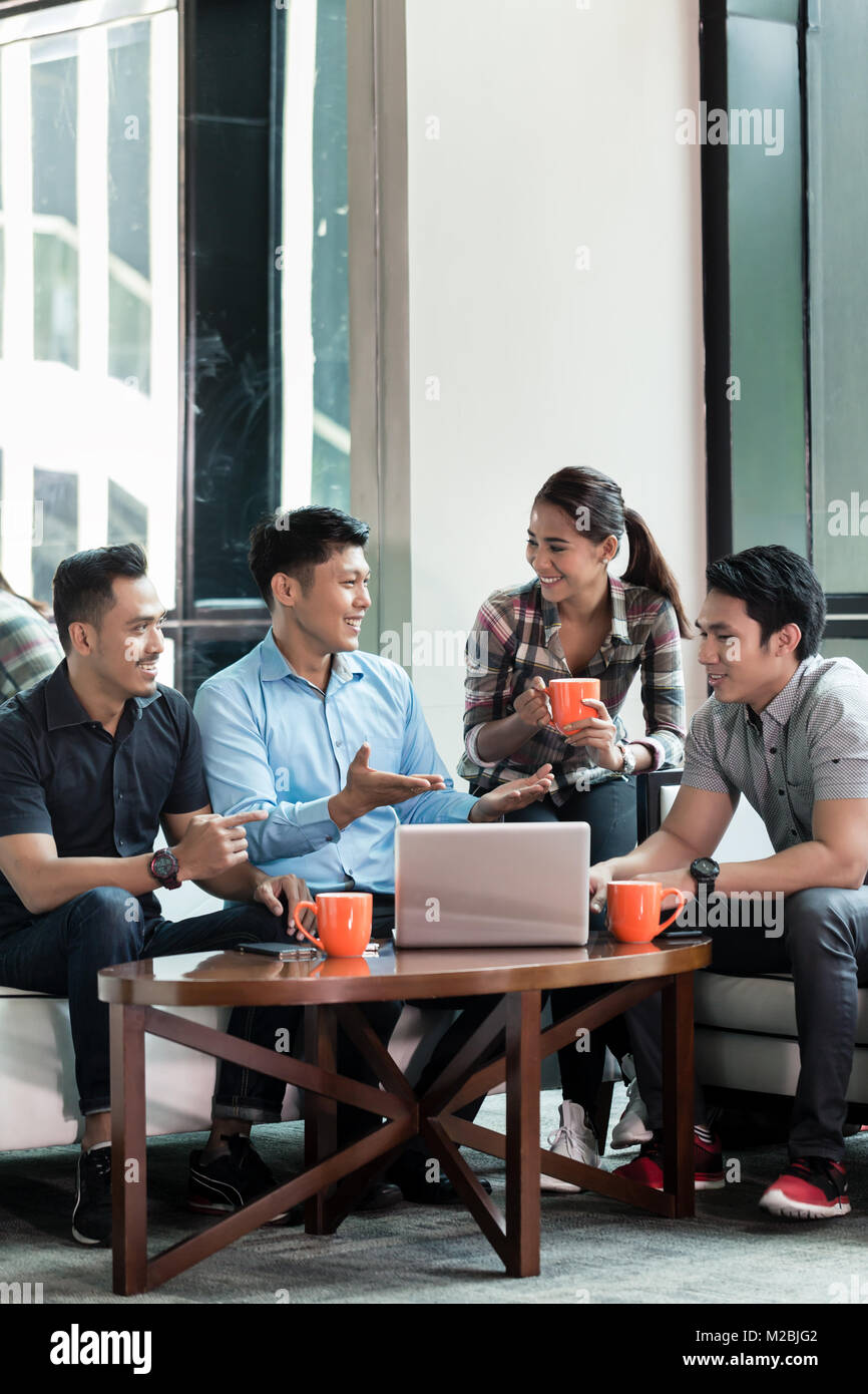 Team of four dedicated employees sitting in front of a laptop while ...