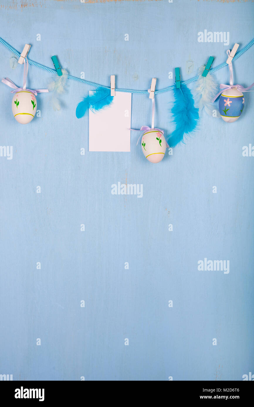 Easter Eggs, feathers and paper on a rope on a blue wooden background ...