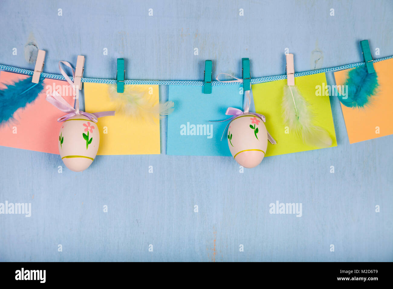 Easter Eggs, feathers and paper on a rope on a blue wooden background ...