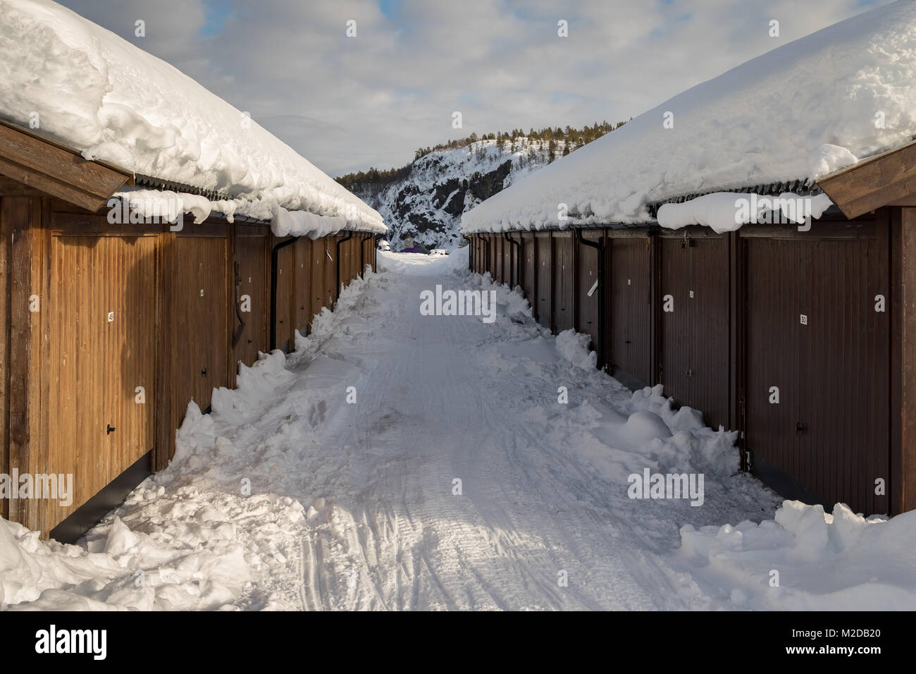 Parallel brown multiple garage buildings, snow on the ground, mountains ...