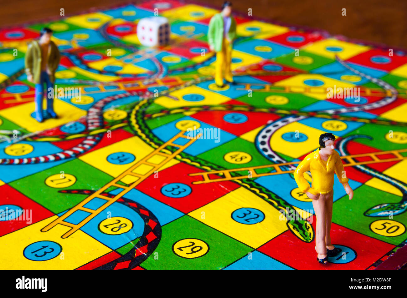 Retro snakes and ladders board with miniature human figures in studio ...