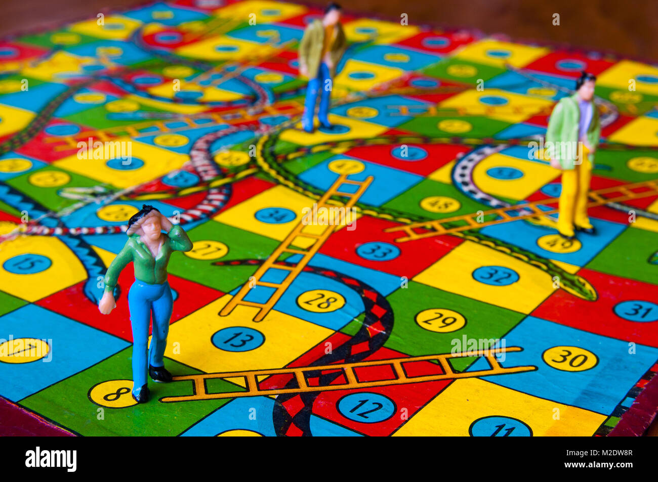 Retro snakes and ladders board with miniature human figures in studio ...