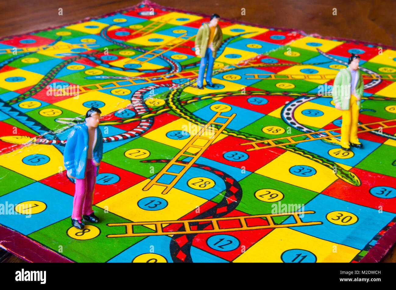 Retro snakes and ladders board with miniature human figures in studio ...