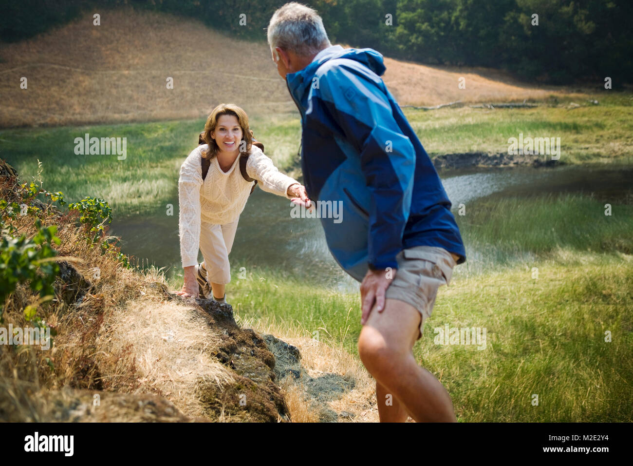 Man pulling arm of woman up hill near lake Stock Photo - Alamy