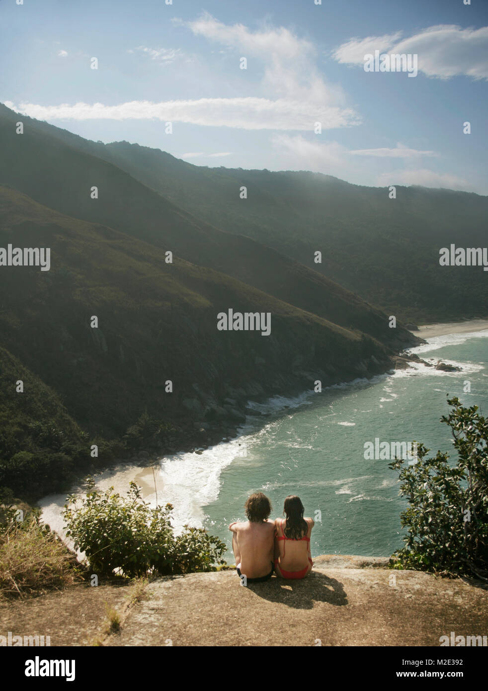 Couple sitting on cliff over ocean beach Stock Photo - Alamy