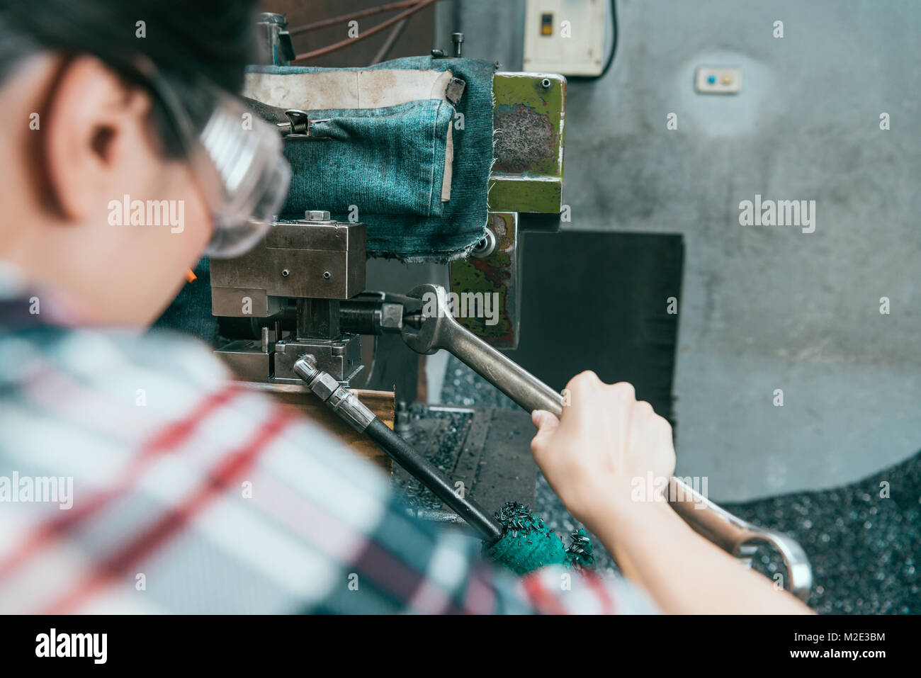 back view of female factory worker wearing safety goggles using wrench ...