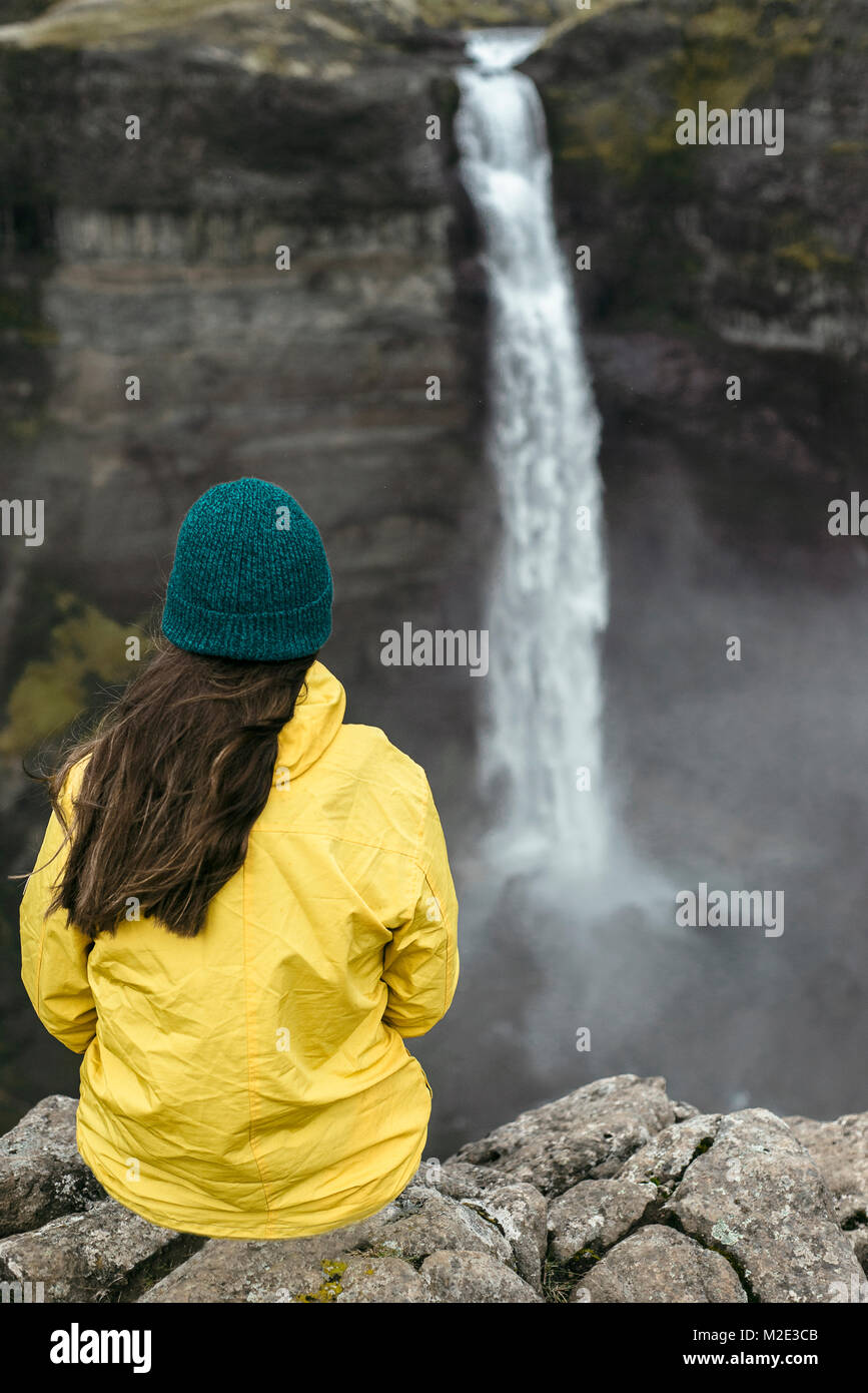 Caucasian woman sitting on cliff admiring waterfall Stock Photo - Alamy