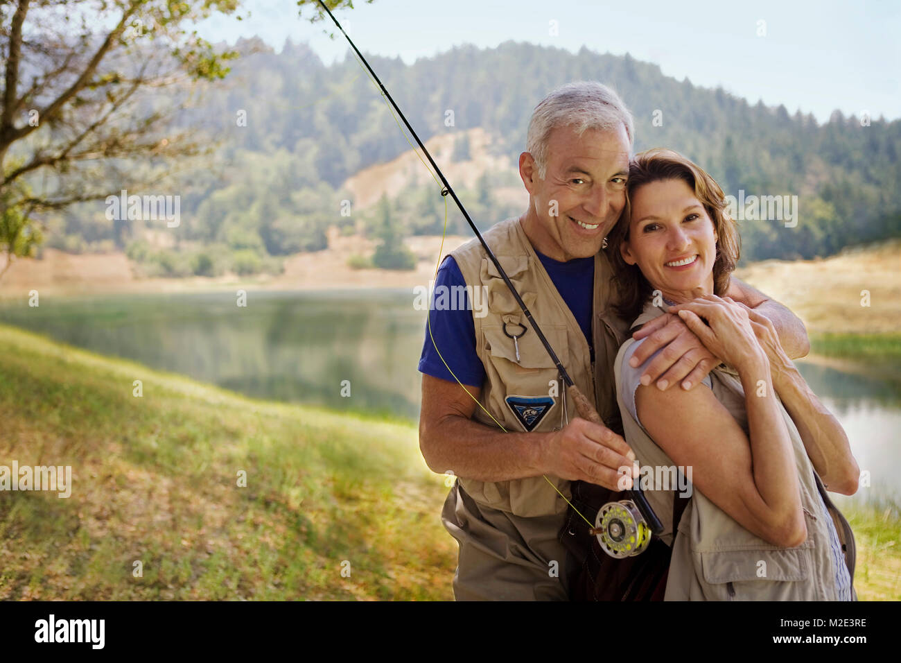 Couple with fishing rod hugging near river Stock Photo - Alamy