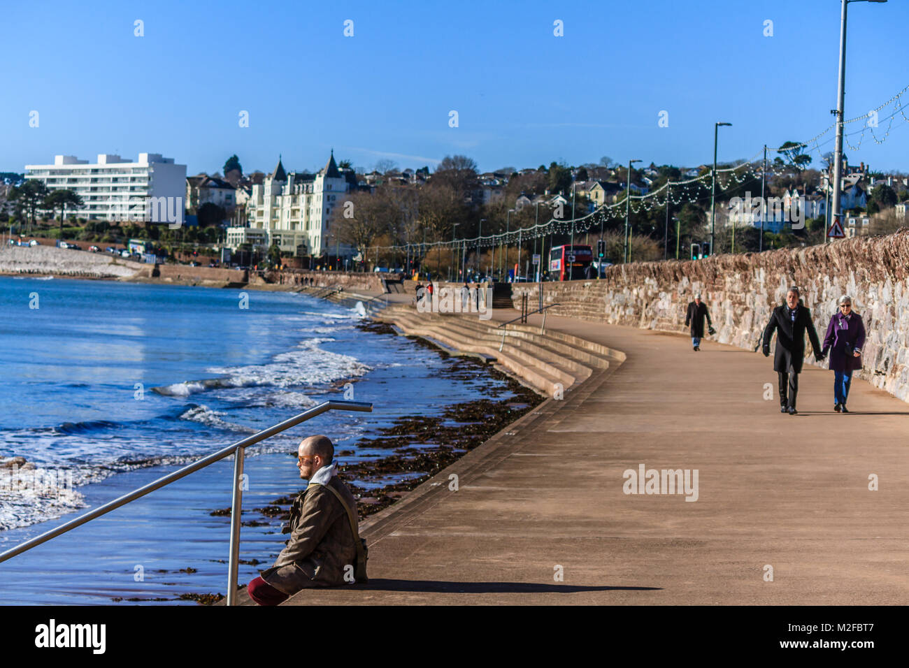 People walking along promenade by Torre Beach at high tide in February ...