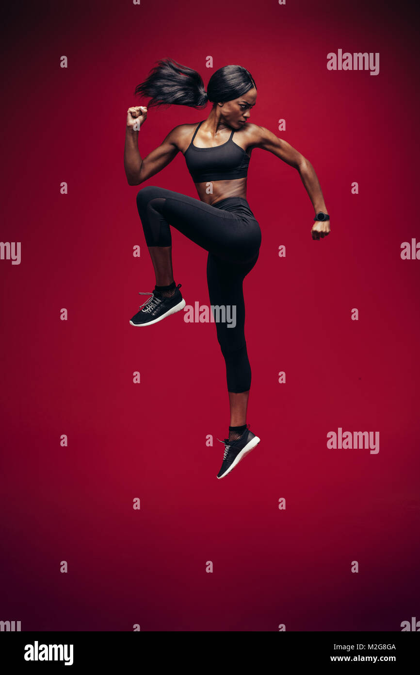 Fitness woman jumping over red background. Full length of healthy young ...