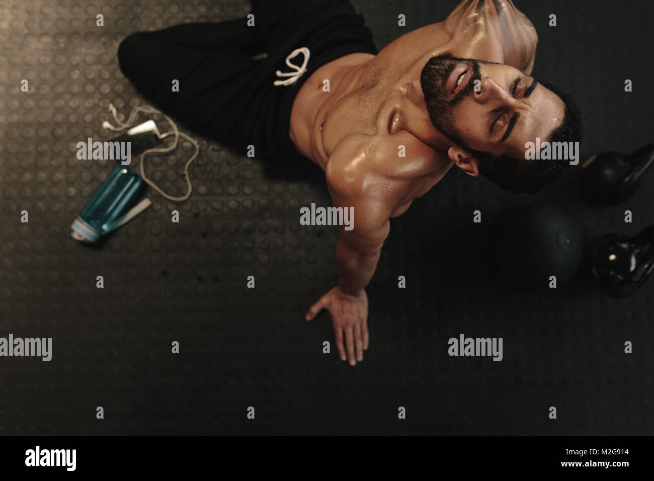 Tired young man sitting on floor and relaxing in gym after training ...