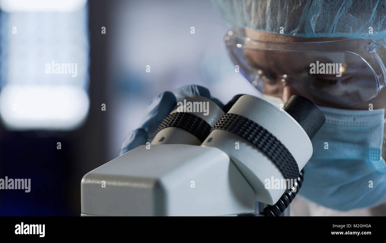 Male scientist in face mask examining biological material, conducting ...