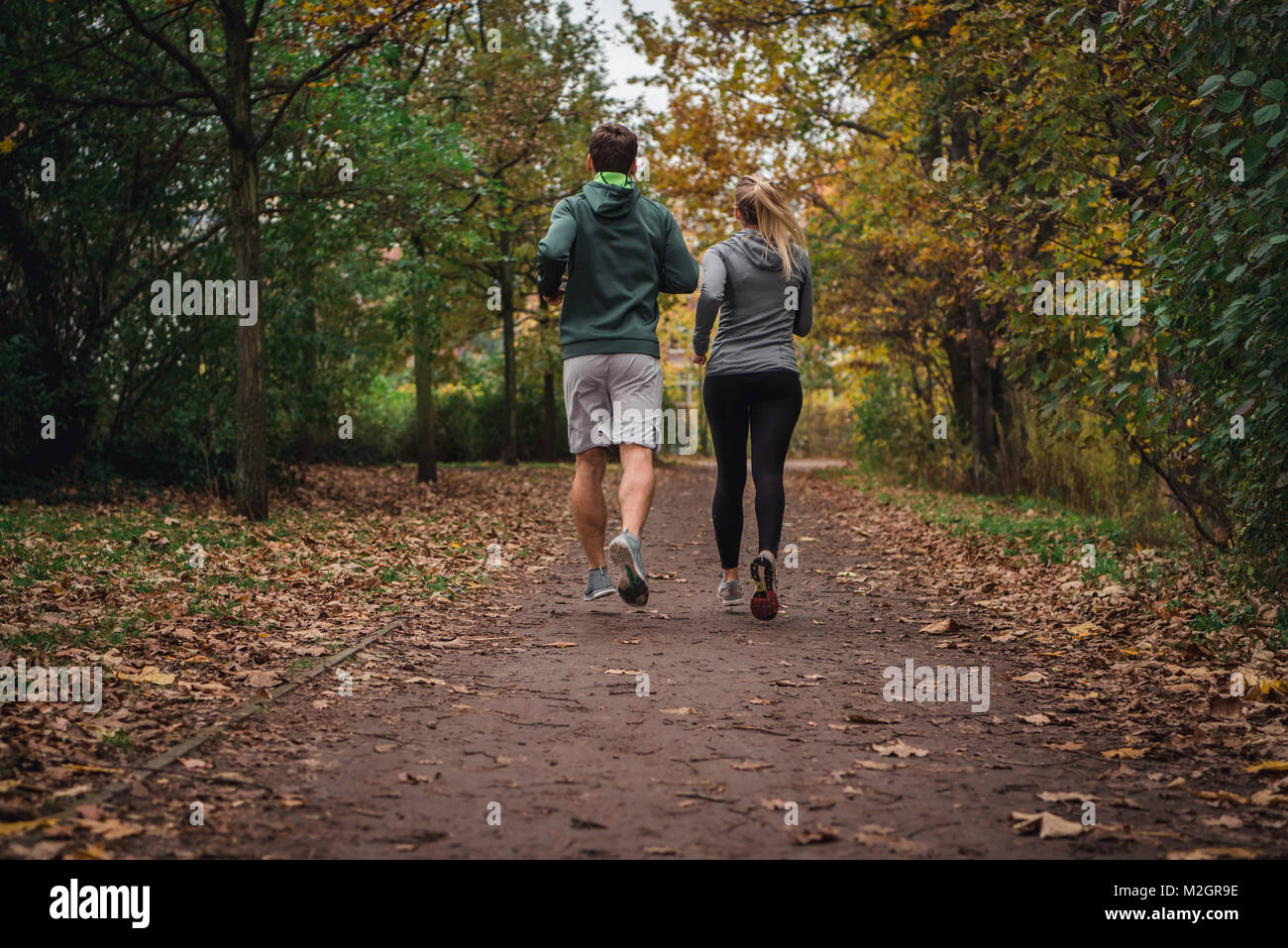 Caucasian man and woman running through the park in the Autumn Fall ...