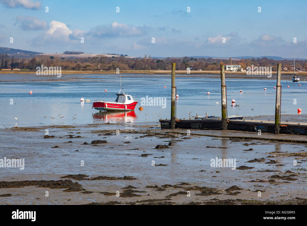 A small red motor boat moored in Chichester Harbour at low tide, at ...
