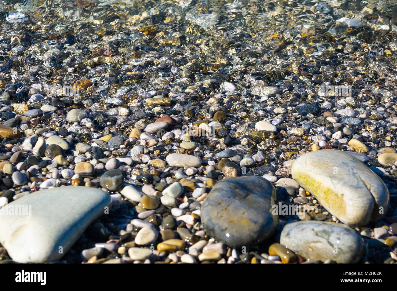 sea pebble beach with multicoloured stones, transparent waves with foam ...