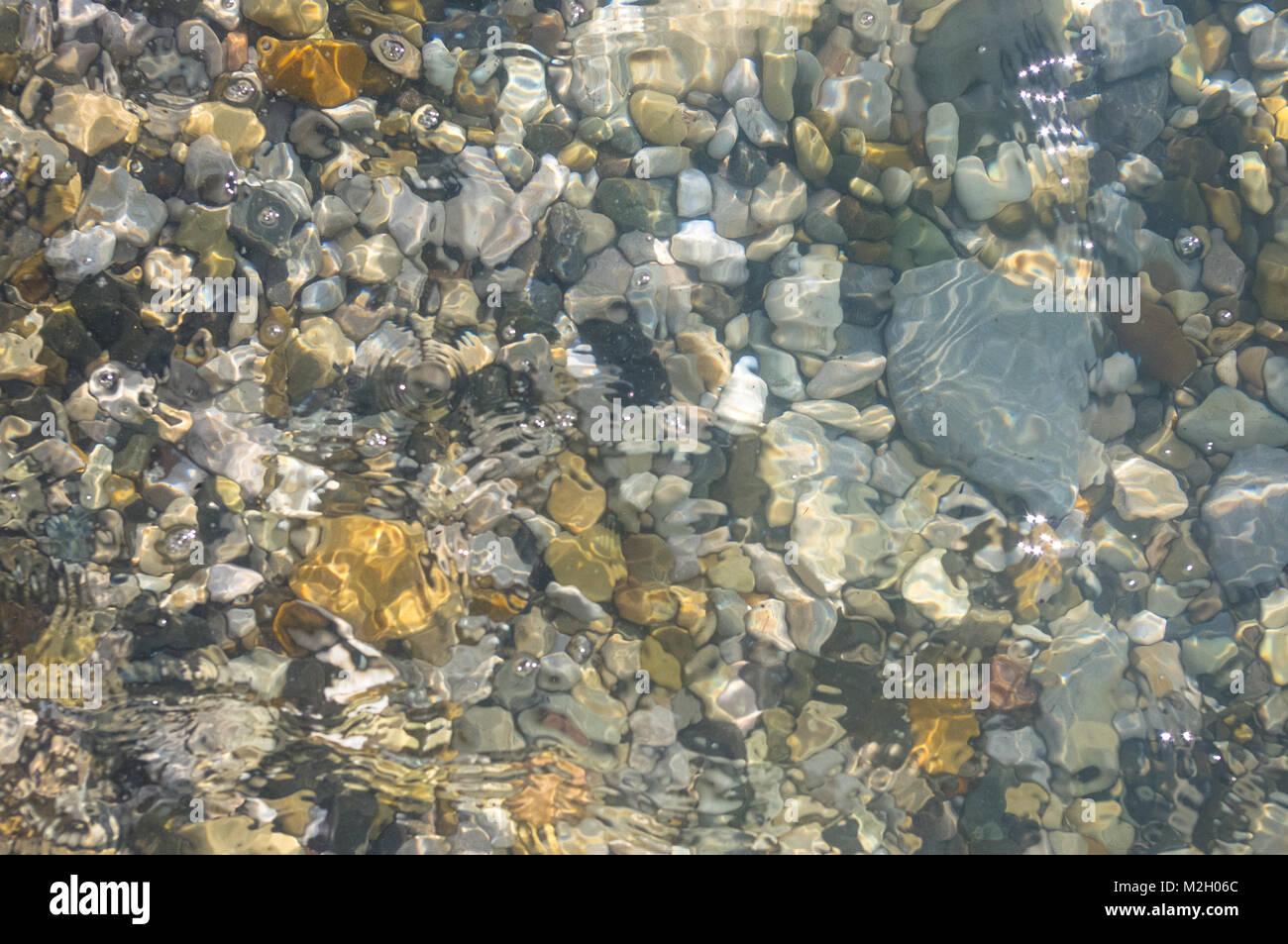 sea pebble beach with multicoloured stones, transparent waves with foam ...