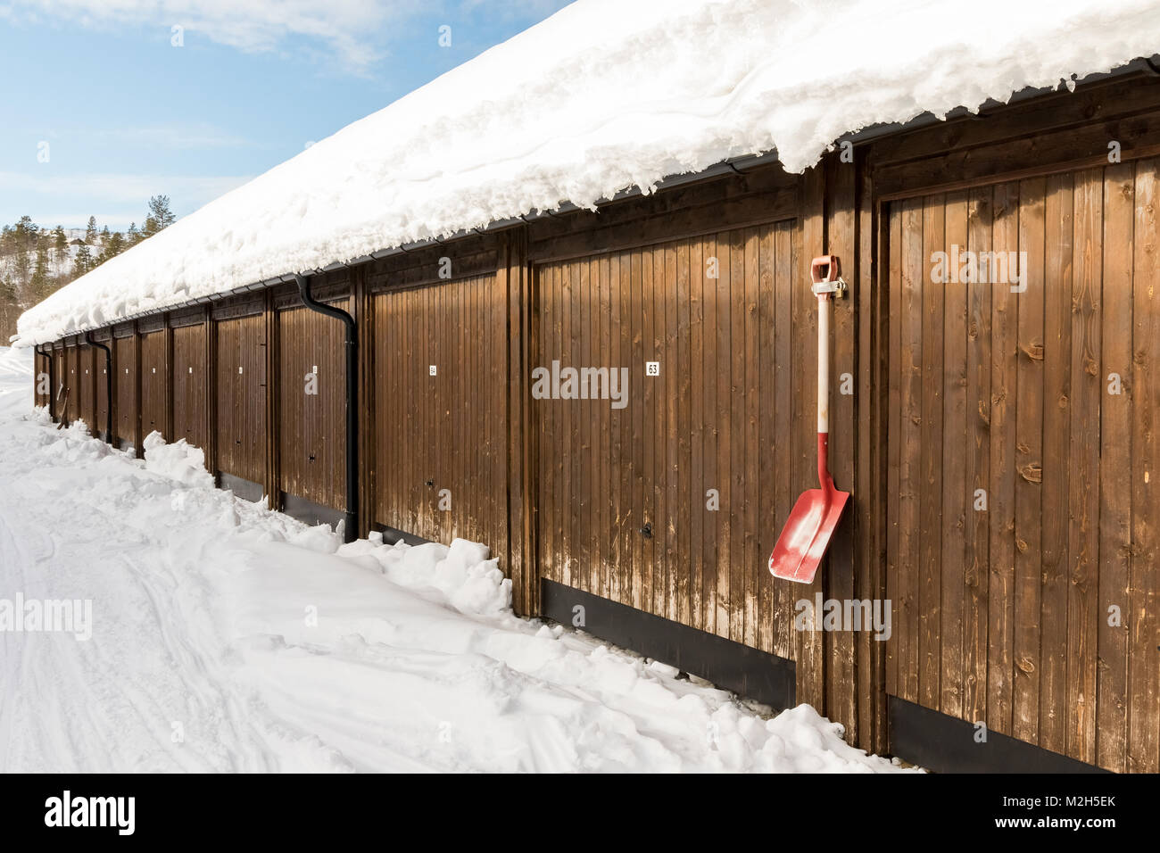 Brown multiple garage building, with a red shovel on the wall, snow on ...