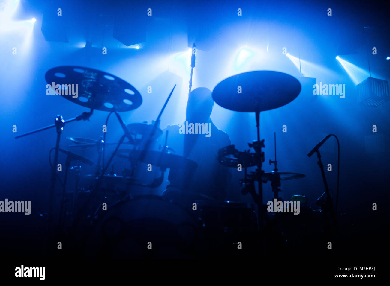 A drummer pictured in silhouette behind his drum kit at a live concert ...