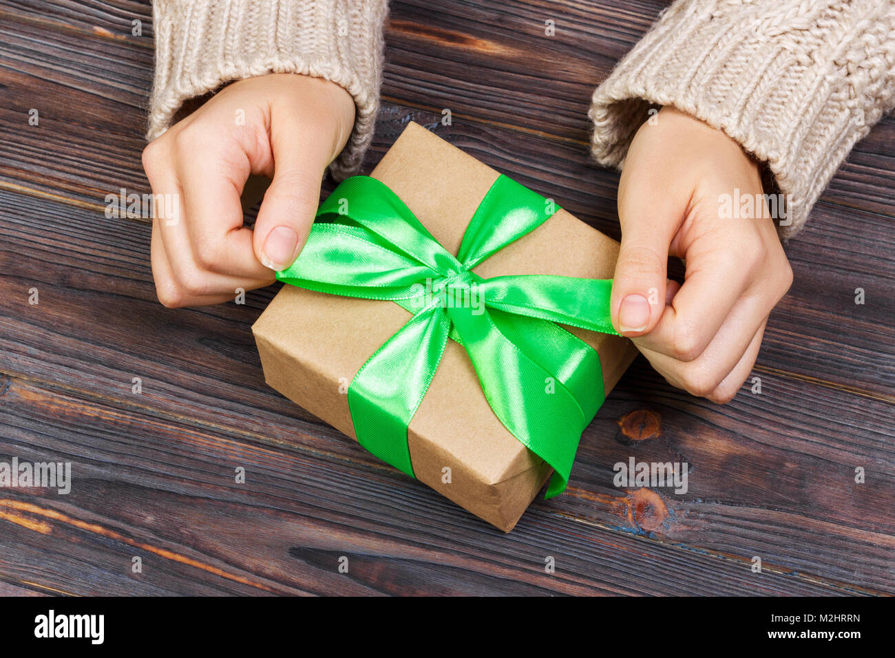 Girl tying a simple green bow on a gift box. Wrapped in plain craft ...