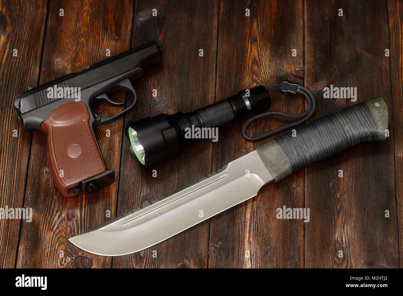 Steel knife, flashlight and gun on a dark wooden background, close-up ...