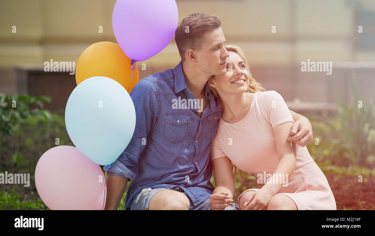 Couple cuddling on bench in summer, guy holding air balloons, romantic ...