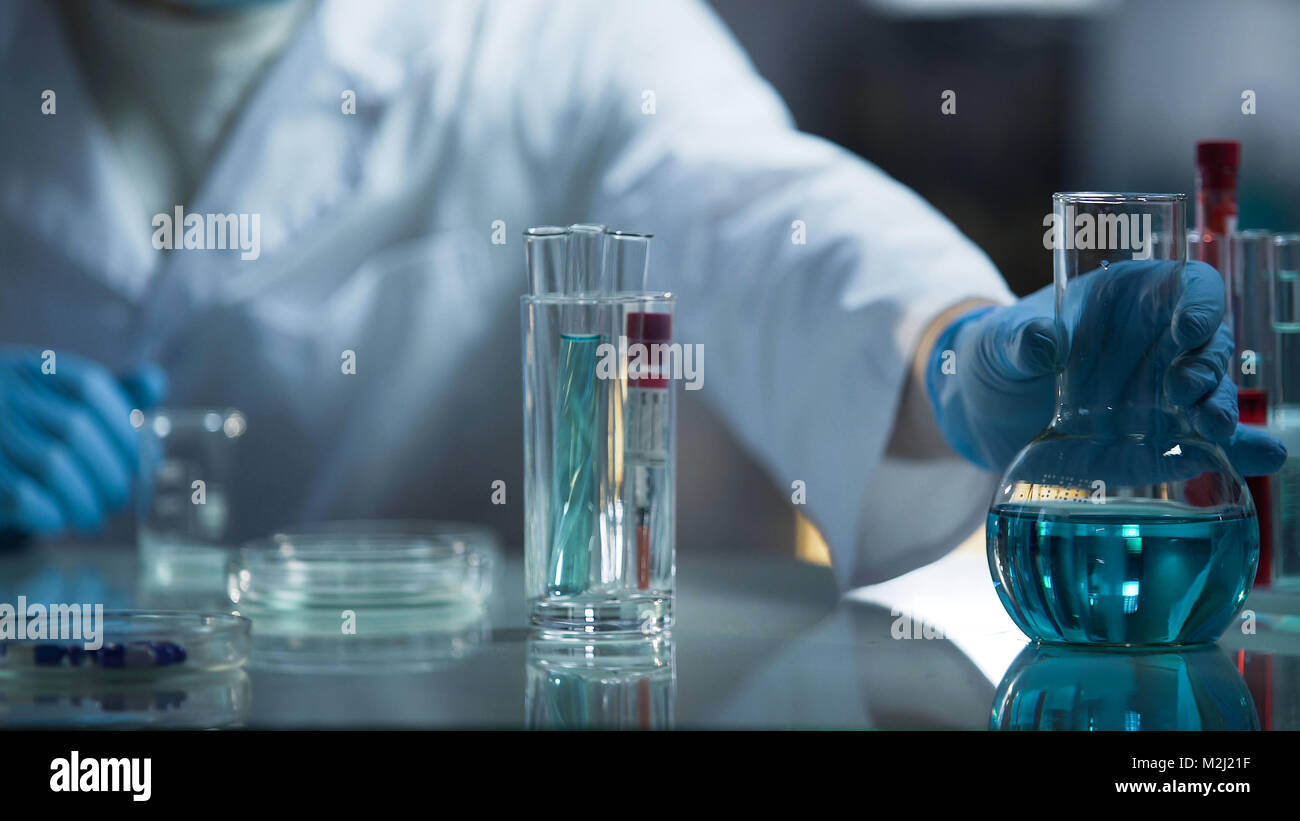 Laboratory worker putting flask with blue reagent on his working ...