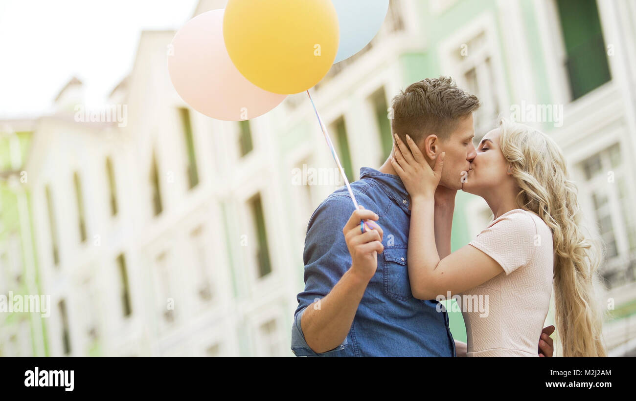 Happy couple with colorful air balloons kissing in street, tender ...