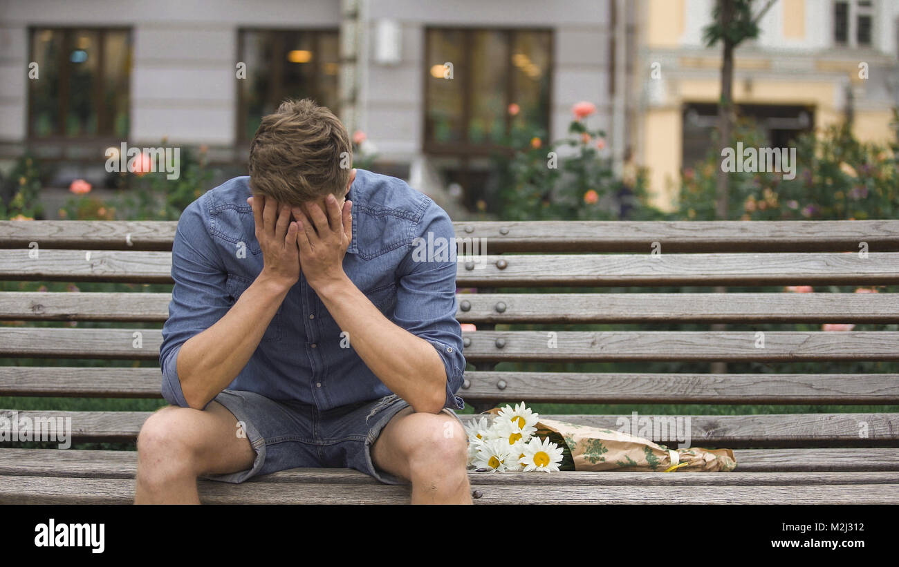 Upset young man sitting on bench alone, closing face with hands, break ...