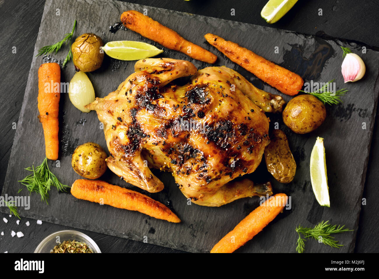 Grilled chicken with vegetables over black stone background. Top view ...