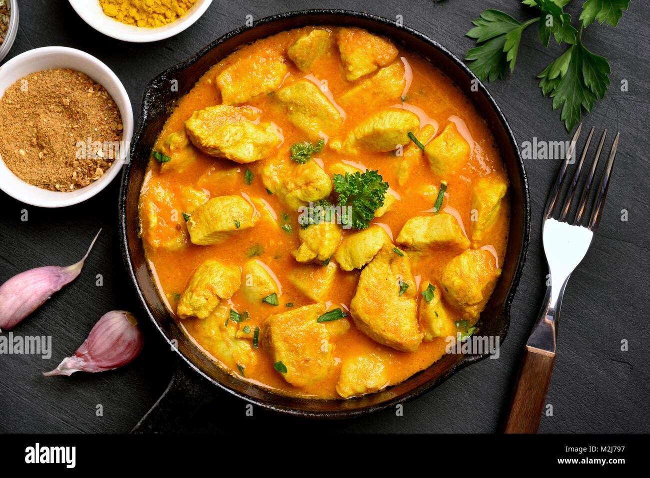 Tasty chicken curry in frying pan on dark stone background. Top view ...